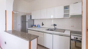 Uma cozinha compacta com armários brancos, uma geladeira de aço inoxidável, uma pia e um fogão.