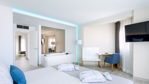 Quarto de hotel moderno com uma cama grande, uma escrivaninha, televisão e banheiro visível por uma porta aberta.