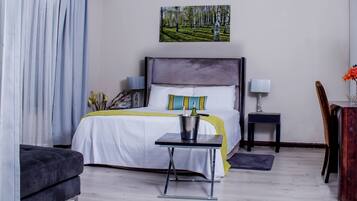 Quarto com cama, mesas de cabeceira, uma pequena mesa, uma cadeira e um quadro na parede.