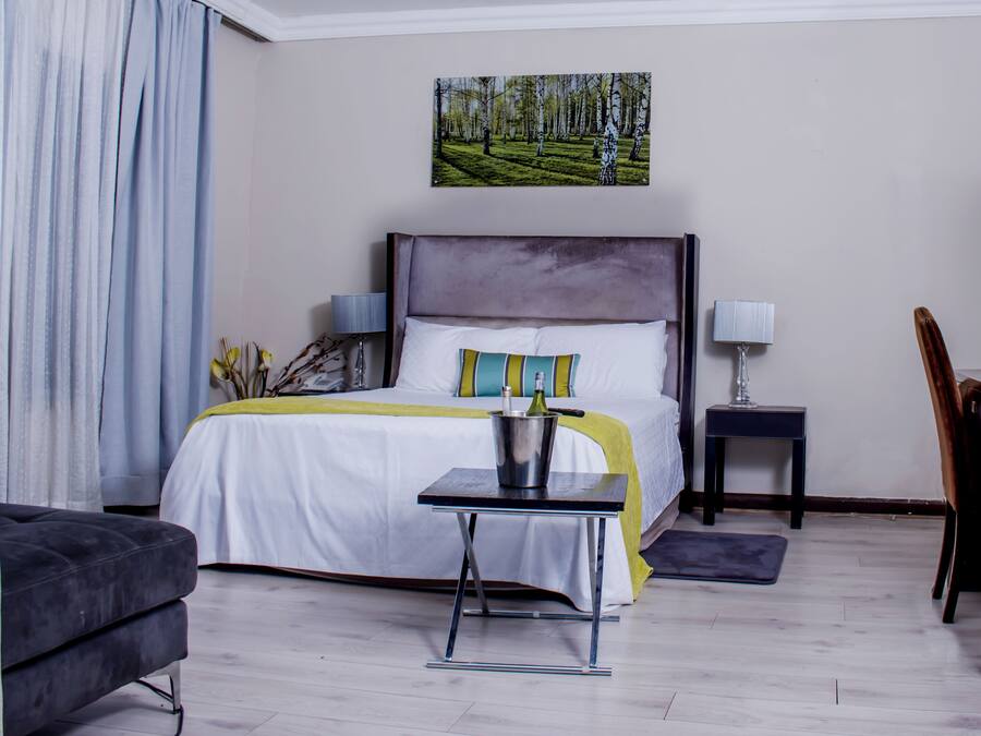 Quarto com cama, mesas de cabeceira, uma pequena mesa, uma cadeira e um quadro na parede.