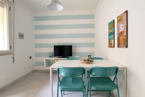 Uma área de refeições com cadeiras verde-água, uma mesa branca e uma TV de tela plana em um suporte.