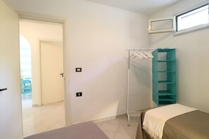 Quarto com cama, guarda-roupa, prateleira e porta que dá para outro espaço.
