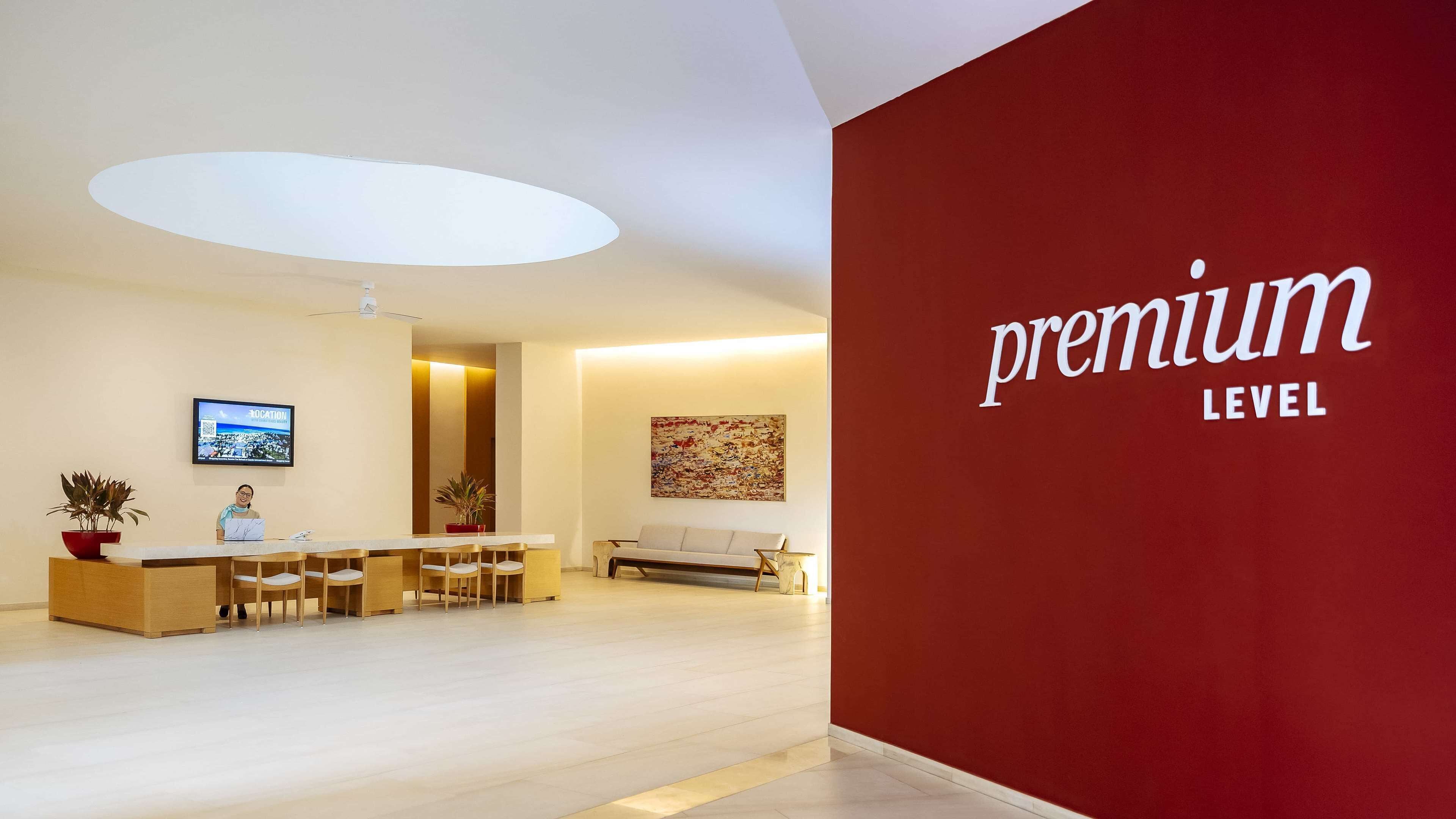 Um hall de hotel moderno, com balcão de recepção, área de estar e uma grande parede vermelha com a sinalização "premium level".