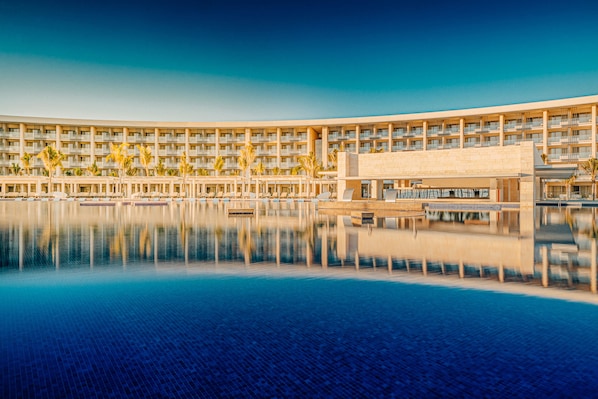 Um hotel grande com piscina em primeiro plano e o reflexo do edifício.