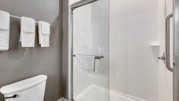 Um banheiro moderno com chuveiro envidraçado, vaso sanitário branco e porta-toalhas com várias toalhas brancas.