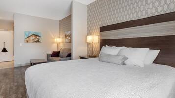 Quarto de hotel moderno com uma cama grande, duas mesas de cabeceira, uma cadeira e um papel de parede estampado.