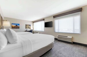 Quarto de hotel com cama grande, escrivaninha, televisão de tela plana e janela com vista para a cidade.