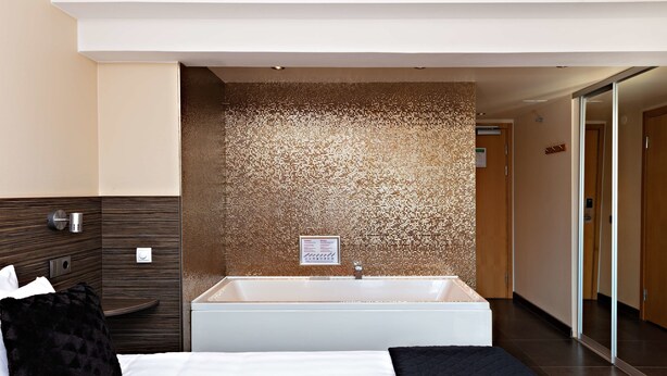 Quarto de hotel moderno com uma cama grande, uma banheira embutida e uma parede de painel de madeira.