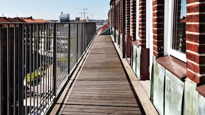 Um deck de madeira com grades de metal, paredes de tijolo e janelas.