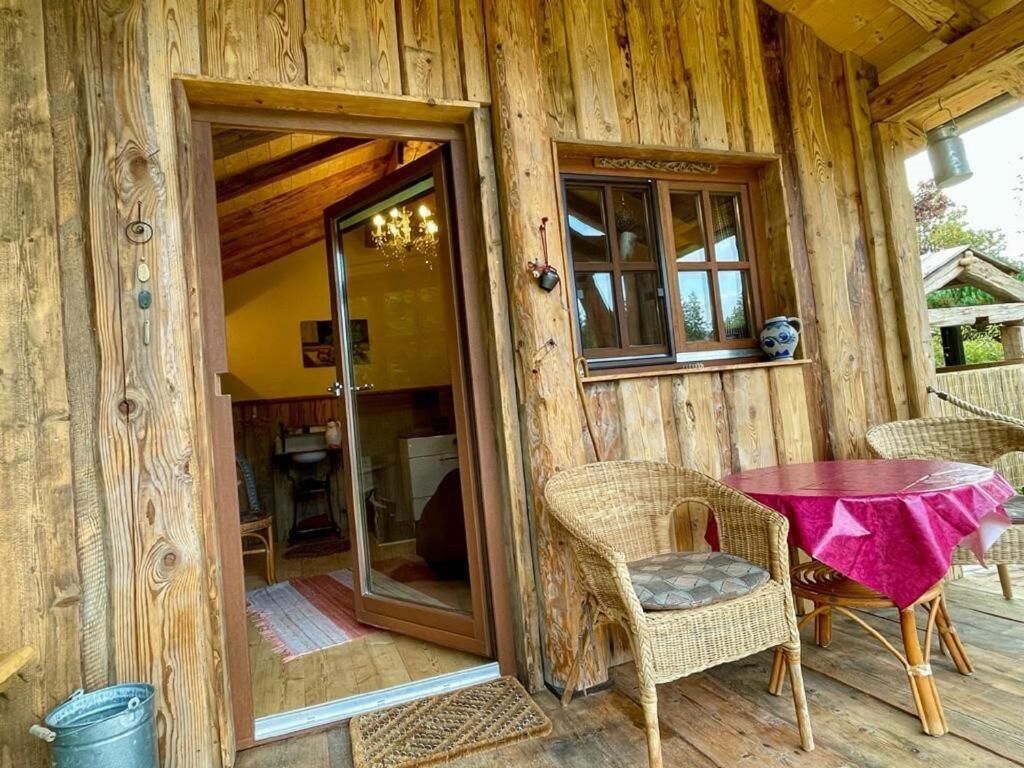 Uma cabana de madeira com porta de vidro, cadeiras de vime e uma mesa coberta por um tecido rosa.