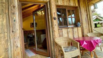 Uma cabana de madeira com porta de vidro, cadeiras de vime e uma mesa coberta por um tecido rosa.