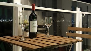 Uma mesa de madeira com duas taças de vinho e uma garrafa de vinho numa varanda à noite.
