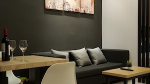 Uma sala de estar moderna com um sofá escuro, uma mesa de jantar de madeira e uma cadeira branca. Há uma obra de arte com um mapa-múndi na parede e um ventilador de teto.