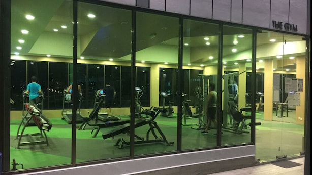 Academia com paredes espelhadas, diversos equipamentos de exercício e um letreiro com a inscrição 'THE GYM'.