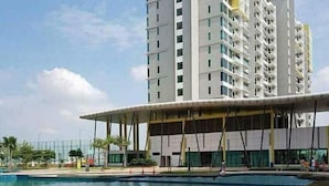 Um hotel moderno com área de piscina, um pavilhão coberto e um edifício alto ao fundo.