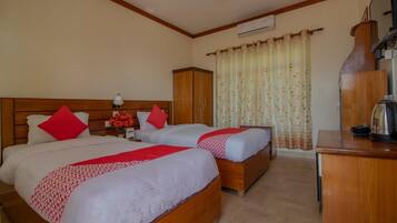 Quarto de hotel com duas camas, cabeceiras de madeira, cômoda de madeira, unidade de ar condicionado e cortina com padrão floral.