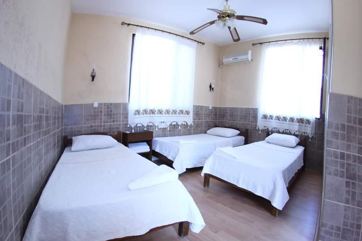 Quarto com três camas de solteiro, ventilador de teto e janela com cortinas.