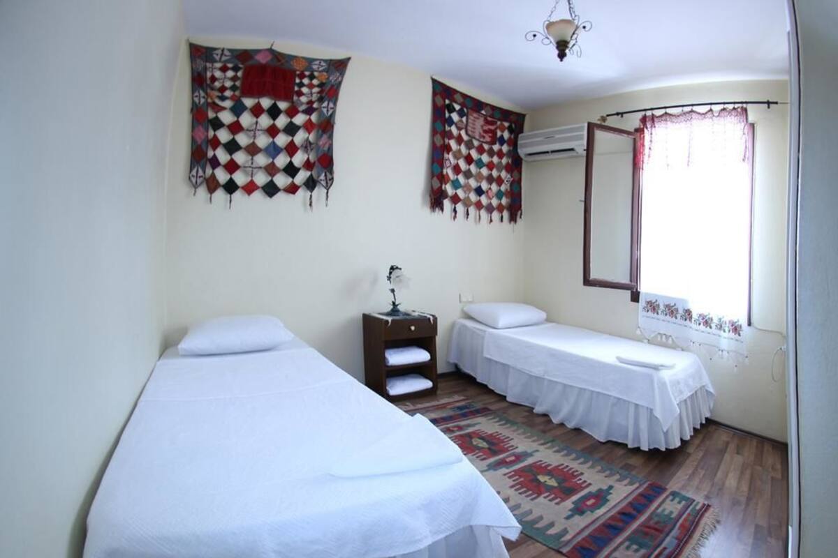 Quarto com duas camas de solteiro, cômoda de madeira, tapete estampado e janela com cortinas.