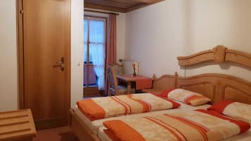 Quarto com duas camas, porta de madeira, escrivaninha e janela com cortinas.