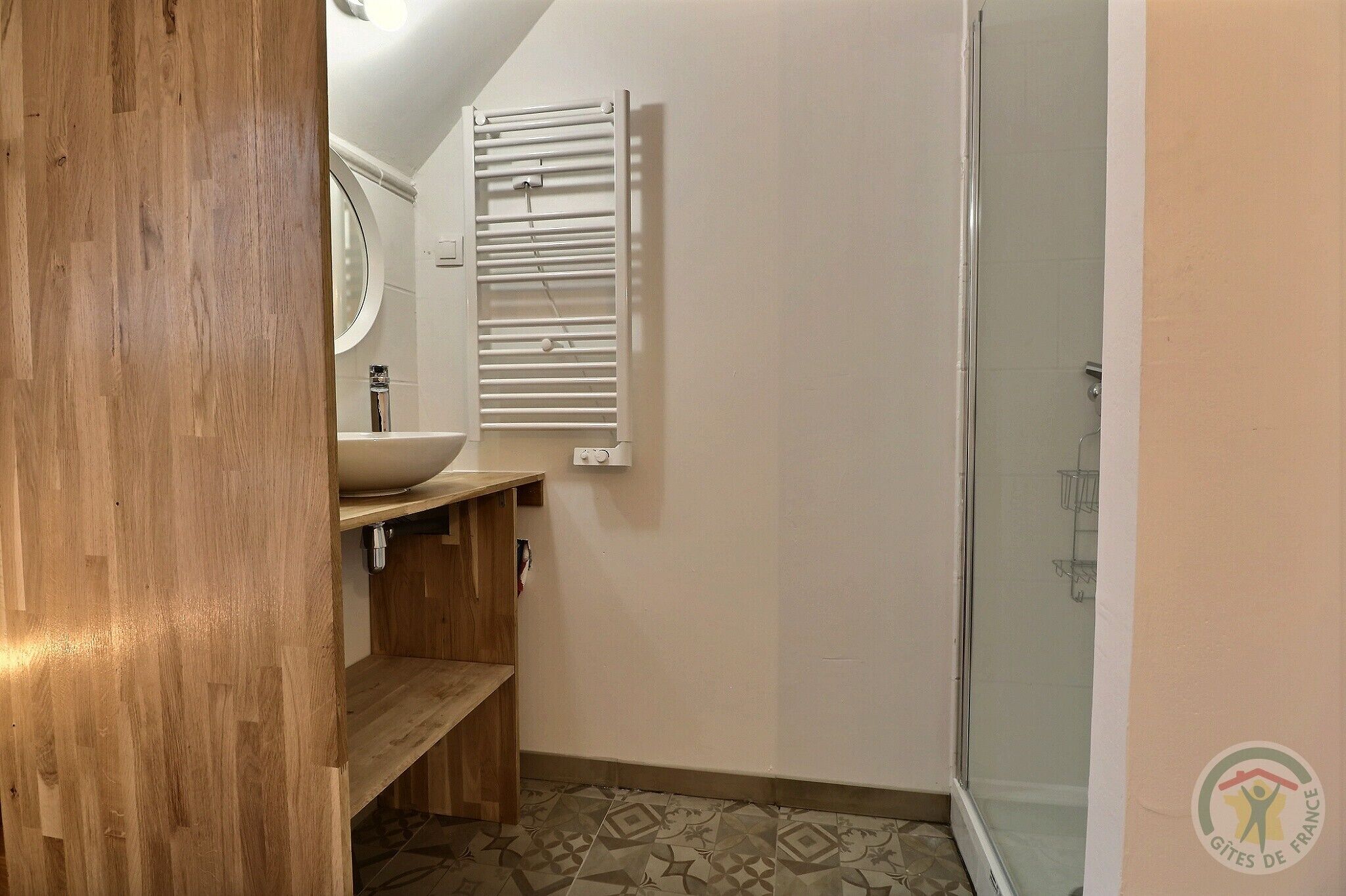 Casa de banho com toucador de madeira, lavatório branco, porta-toalhas e cabine de duche em vidro.