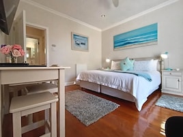 Quarto com cama, mesas de cabeceira, escrivaninha e espelho.