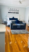 Uma sala de estar moderna com um sofá cinzento, uma cabeceira branca e um ventilador de teto.