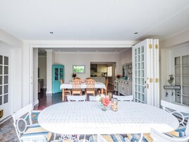 Uma área de refeições com uma mesa redonda, cadeiras e uma cozinha ao fundo.