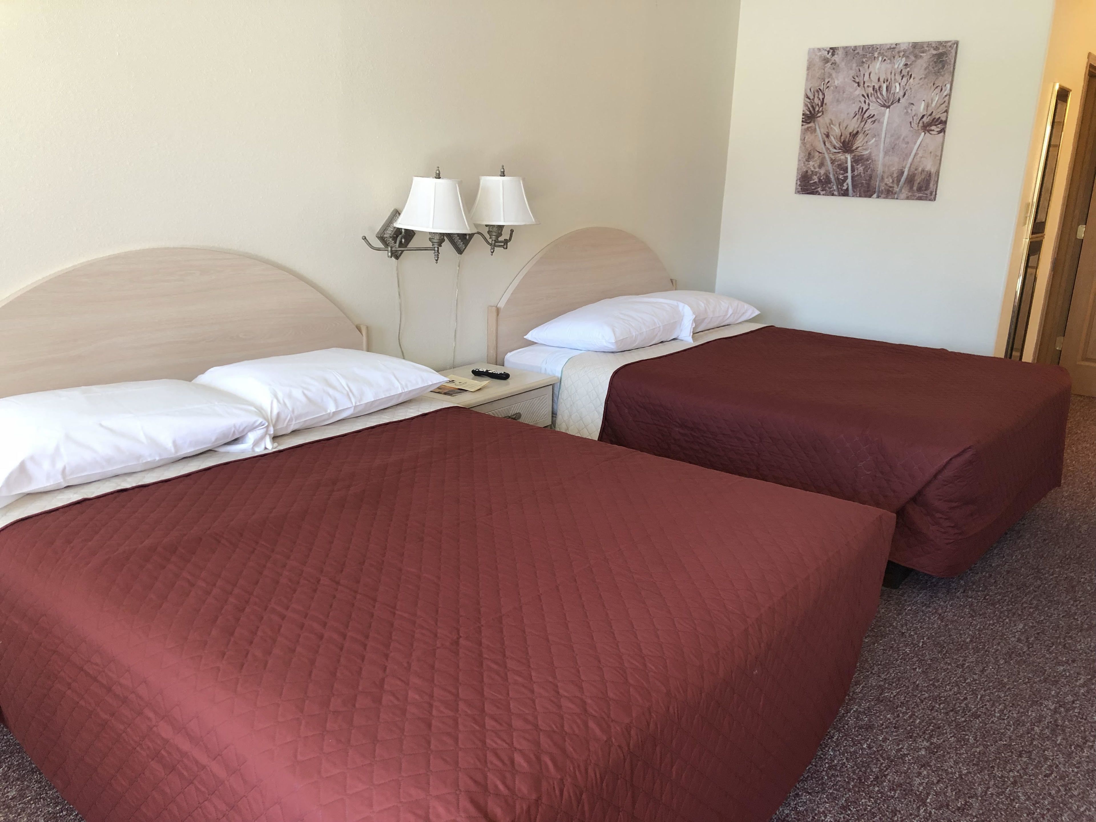 Quarto de hotel com duas camas, cada uma com colcha acolchoada vermelha e almofadas brancas. Há duas luminárias fixadas na parede na mesinha de cabeceira entre as camas.