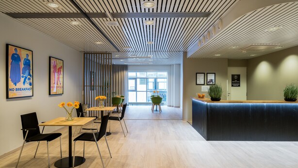 Uma área de recepção moderna com um balcão de madeira, cadeiras pretas e um painel de vidro.