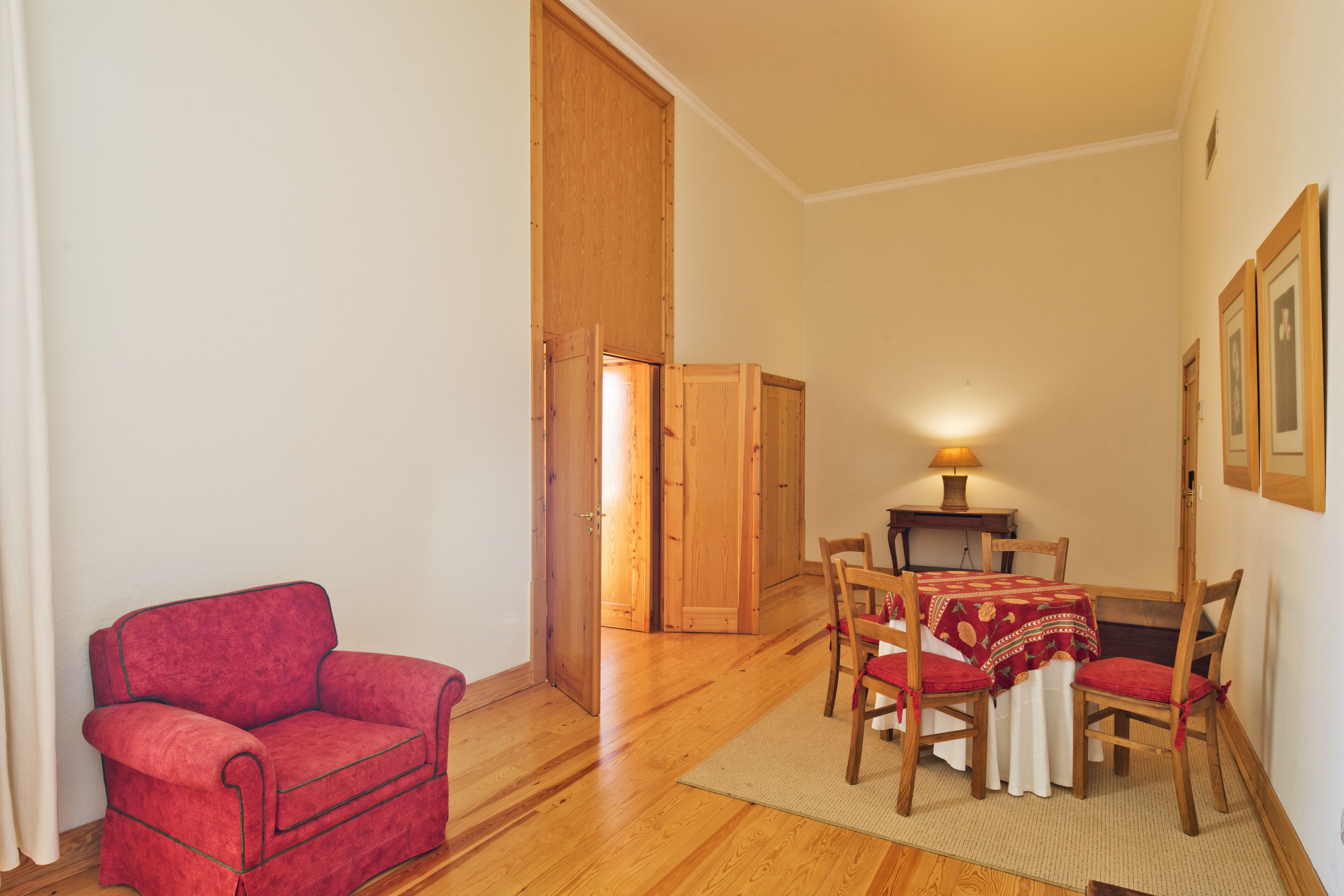 Quarto com poltrona vermelha, mesa de jantar com cadeiras, armários de madeira e uma luminária.