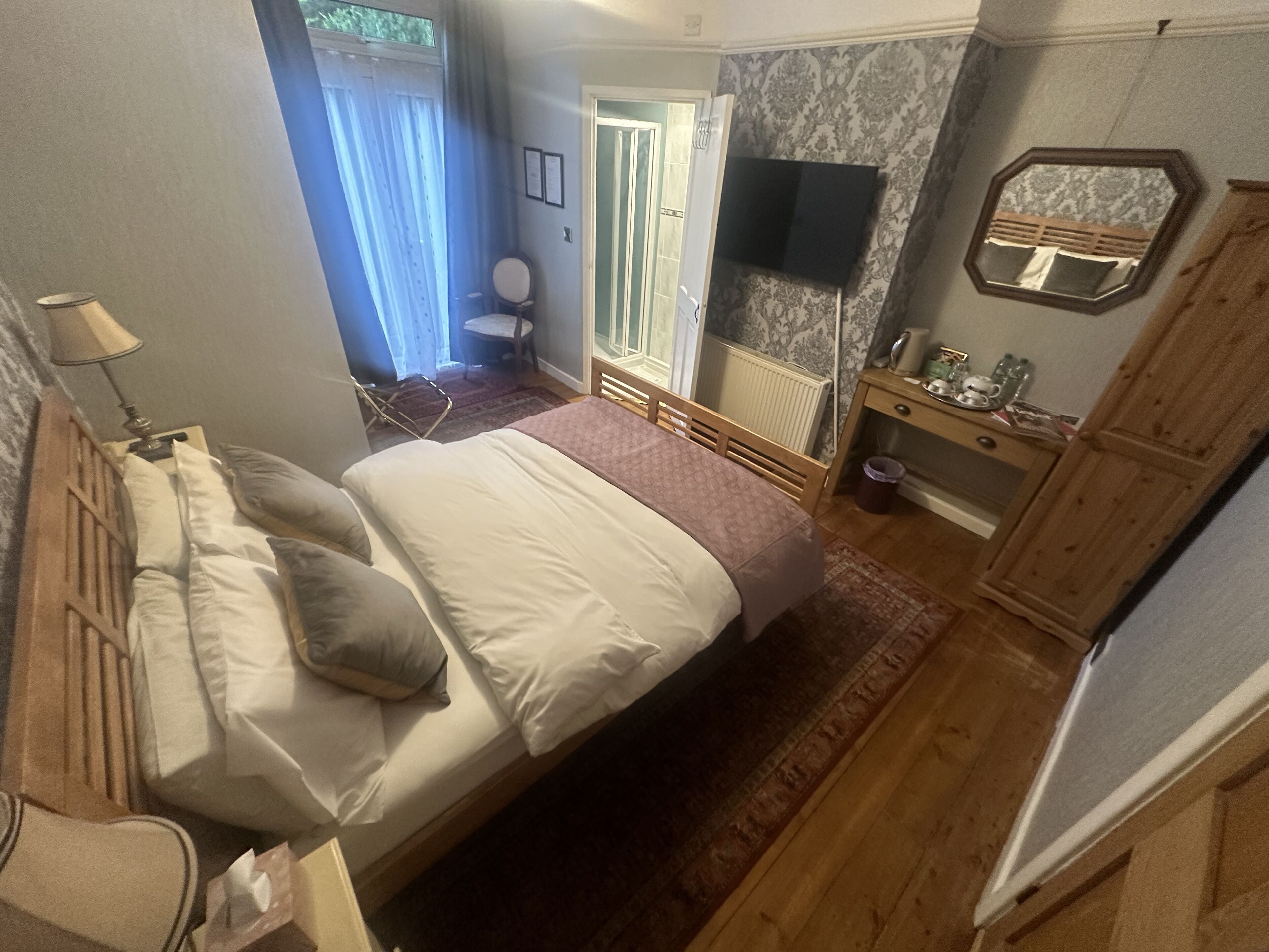 Quarto com cama, penteadeira, espelho, televisão e porta para um banheiro.