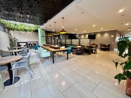 Um café moderno com diversas opções de assento, incluindo mesas e cadeiras, uma ilha central com bancada e luminárias pendentes no teto.