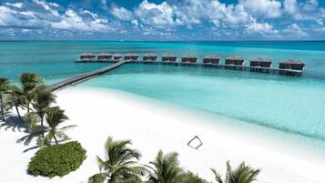 Um resort à beira-mar com bangalôs sobre a água, uma praia de areia branca e águas turquesa cristalinas.