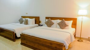 Duas camas de solteiro com cabeceiras de madeira, roupa de cama branca e almofadas estampadas. Um abajur está localizado à direita.