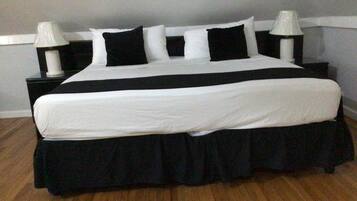 Cama bem arrumada com colcha preta e branca, com duas mesas de cabeceira e luminárias ao lado.