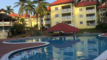 Um resort com piscina, edifícios de vários andares com varandas e palmeiras.