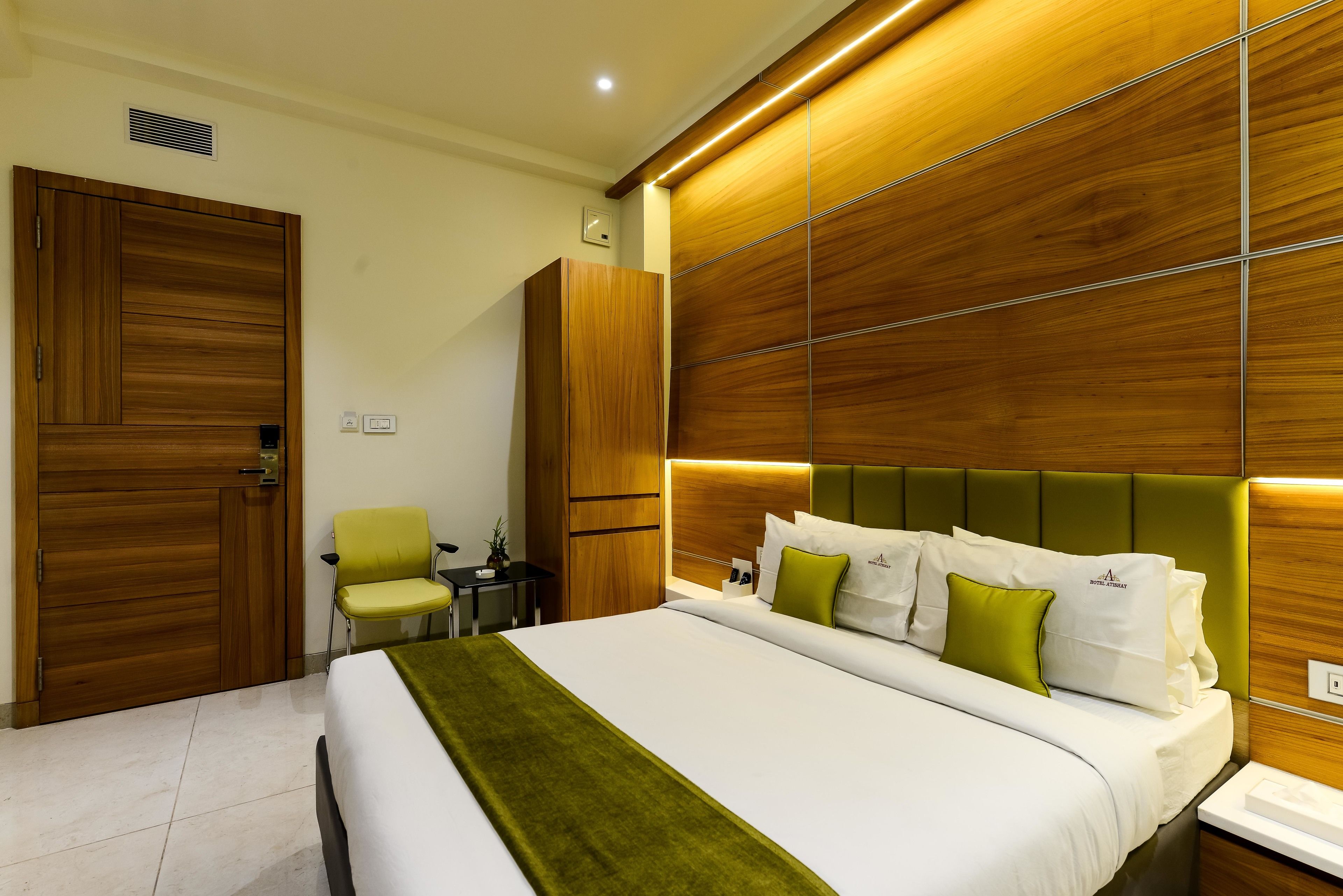 Quarto de hotel com uma cama grande, cabeceira de madeira e uma parede verde de destaque.