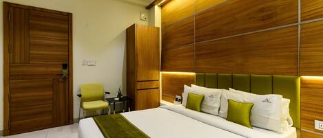 Quarto de hotel com uma cama grande, cabeceira de madeira e uma parede verde de destaque.