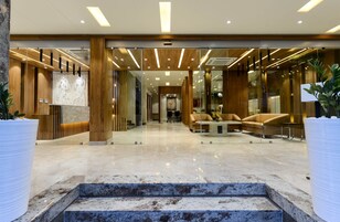 Um lobby moderno com piso de mármore, detalhes em madeira e área de estar com sofás e uma mesa de centro.