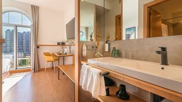 Quarto de hotel moderno com uma janela grande, uma escrivaninha de madeira, uma pia branca e um espelho.