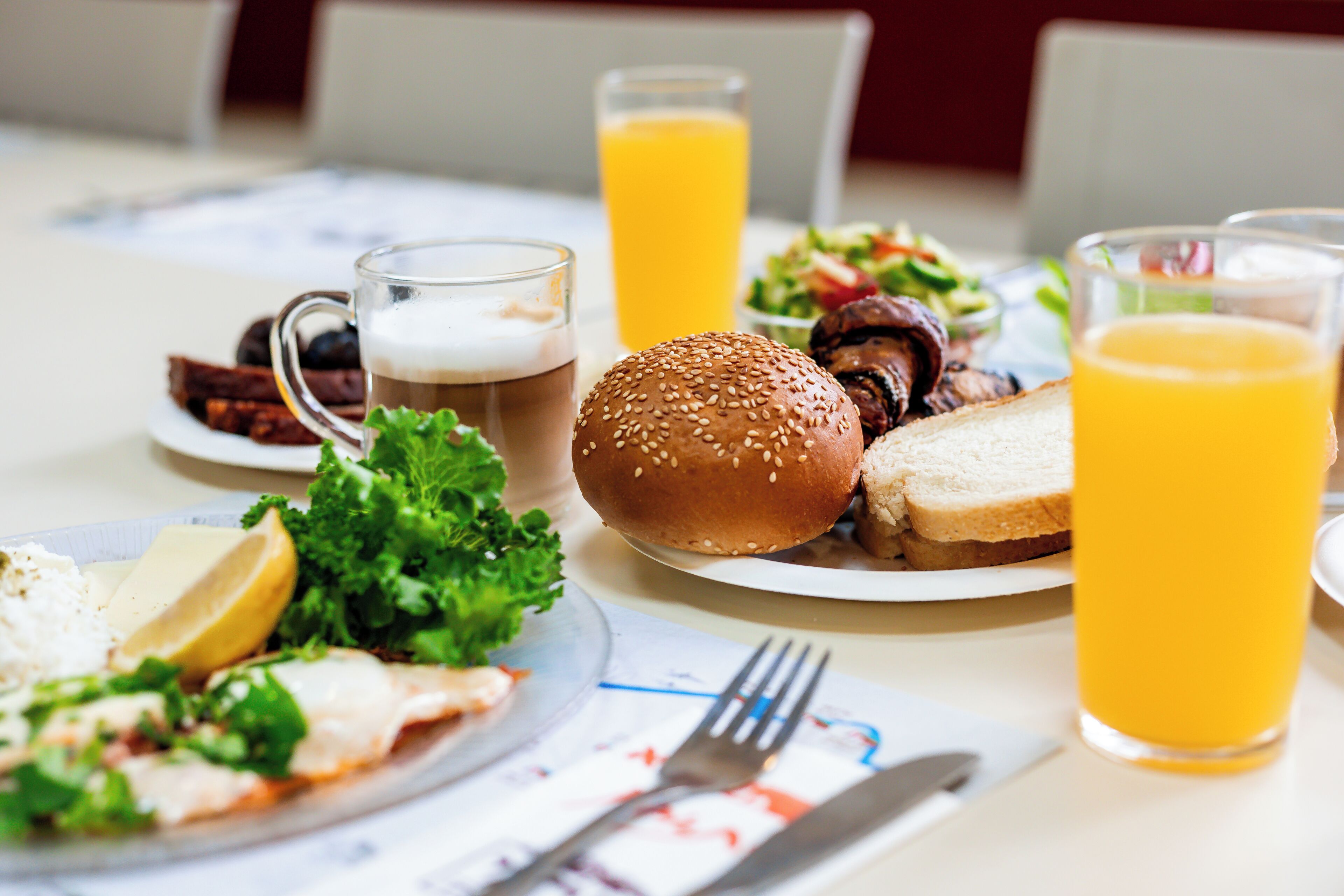 Uma mesa de jantar com pratos de comida, copos de suco de laranja e um copo de cerveja.