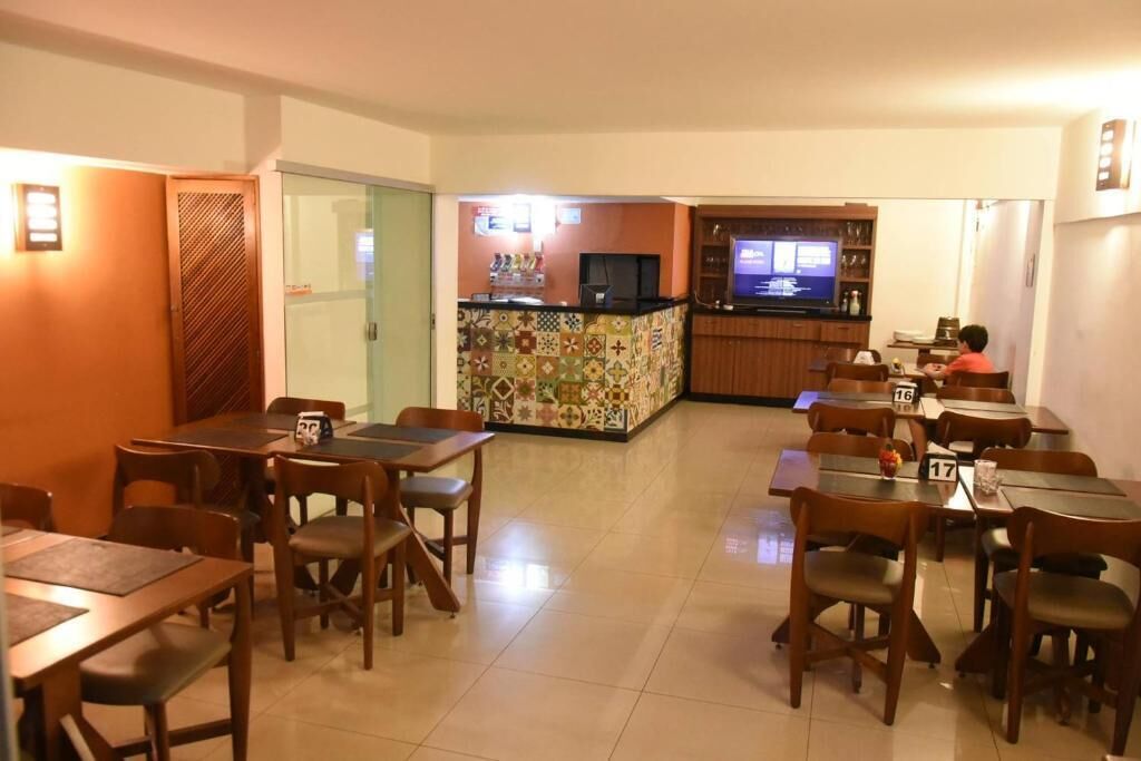 Um restaurante com várias mesas e cadeiras, um balcão com uma televisão e chão em mosaico.