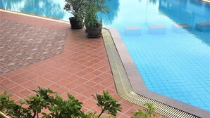 Piscina com deck revestido, plantas em vasos e espreguiçadeiras.