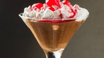 Uma sobremesa em taça martini, com chantilly e cerejas por cima.
