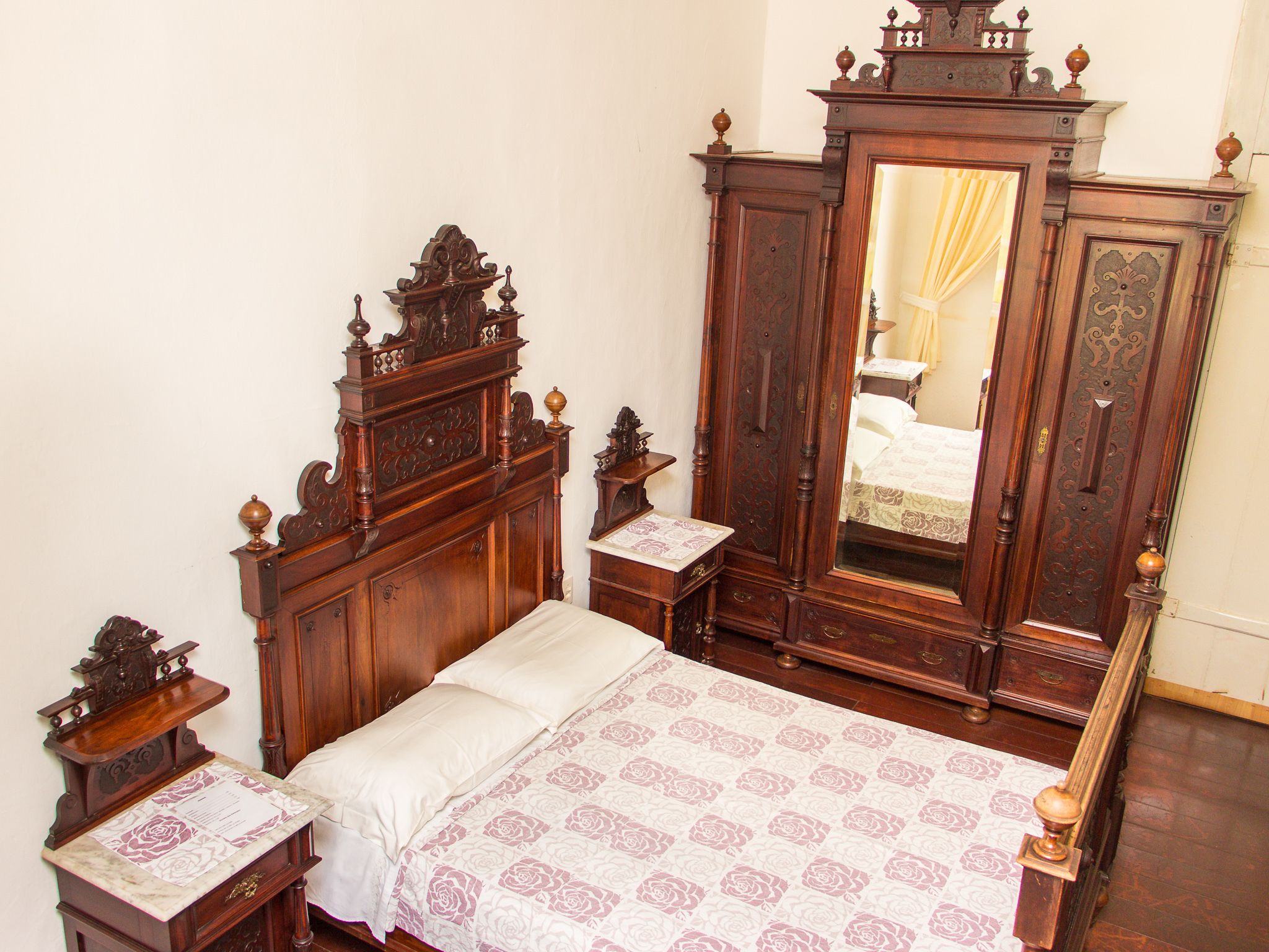 Um quarto tradicional com uma cama de madeira, um espelho grande e um guarda-roupa.