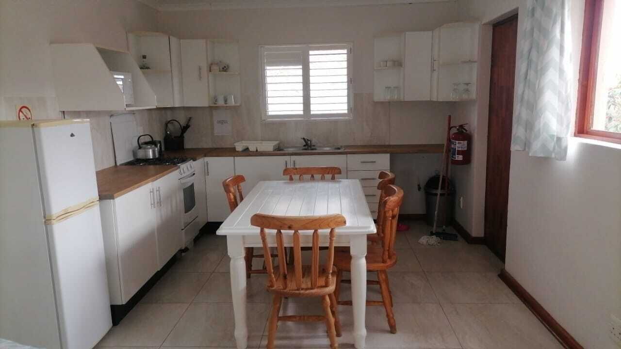 Uma cozinha com armários brancos, uma mesa de jantar com cadeiras, uma janela e um extintor de incêndio.
