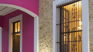 Um edifício com fachada rosa, porta branca e janela com grades de ferro decorativas.