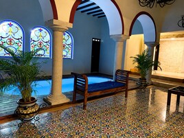 Uma área de piscina com um banco, colunas e piso revestido.