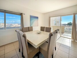 Uma área de refeições com mesa, cadeiras, janelas amplas e um quadro na parede.