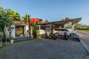 Um prédio com uma placa que diz 'GUNG WIWIN HOME STAY'. Motocicletas estão estacionadas na frente, e um carro está estacionado ao lado.